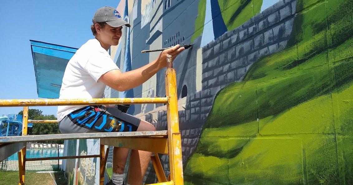 Student painting mural on wall of Lytle Pool bathhouse in Mattoon