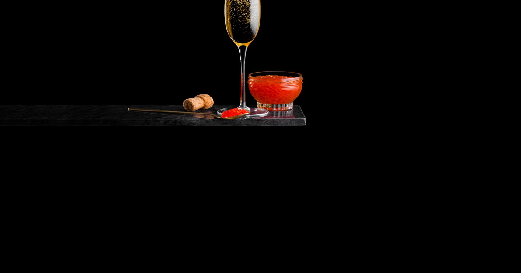 Elegant glass of yellow champagne with red caviar on golden spoon and ...
